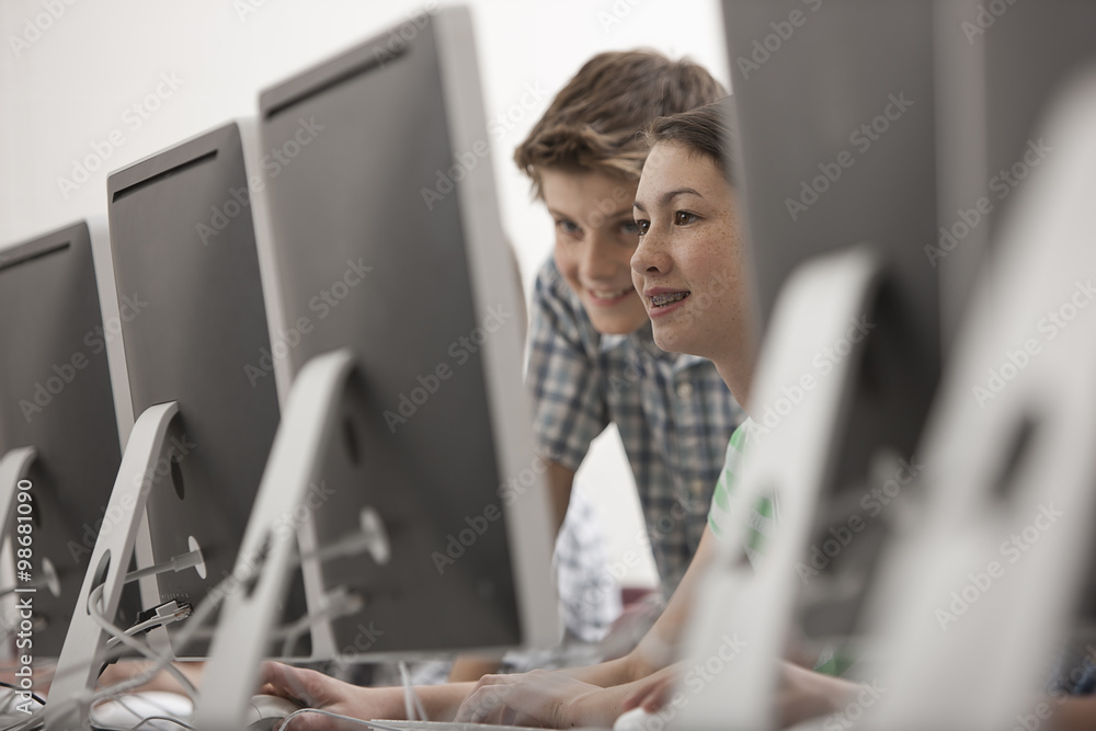 A school computer lab room, with rows of screens. Two young people ...
