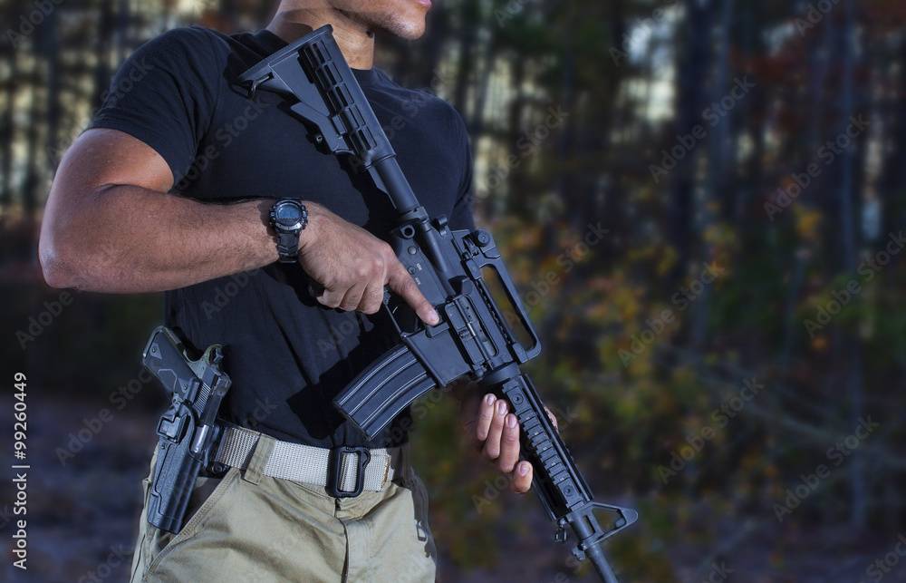 Man in a forest holding an assault rifle with handgun on his side ready ...