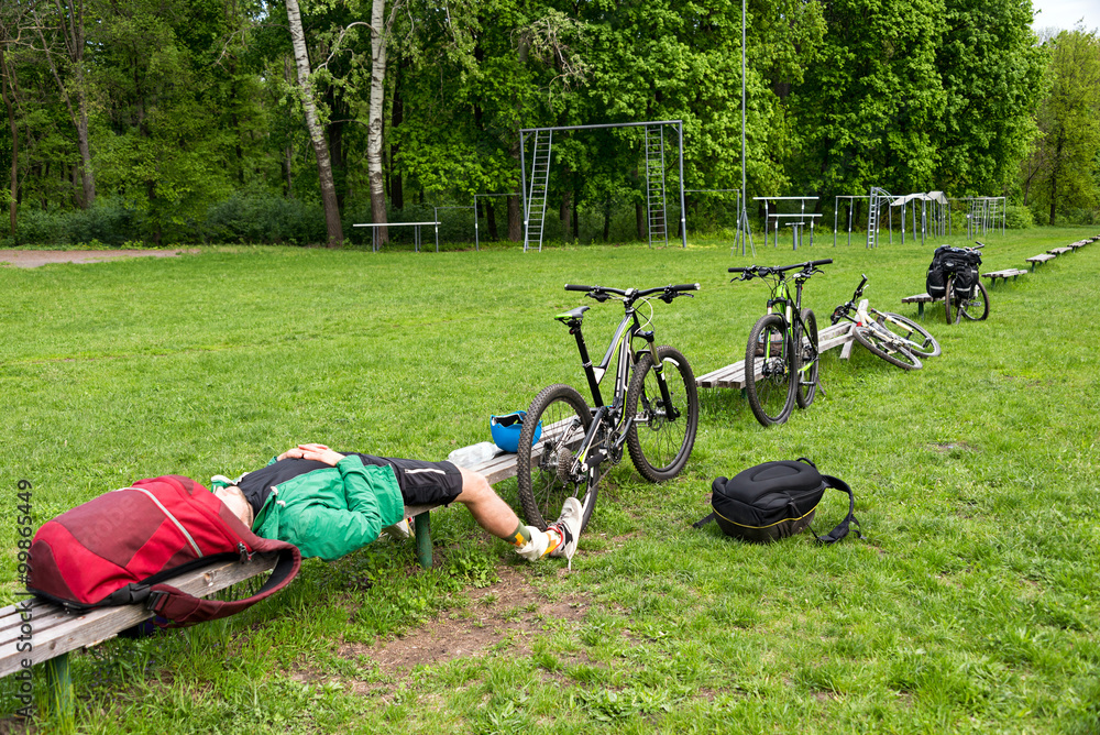 Cyclist resting on a bench in the park. Tired young man with his ...