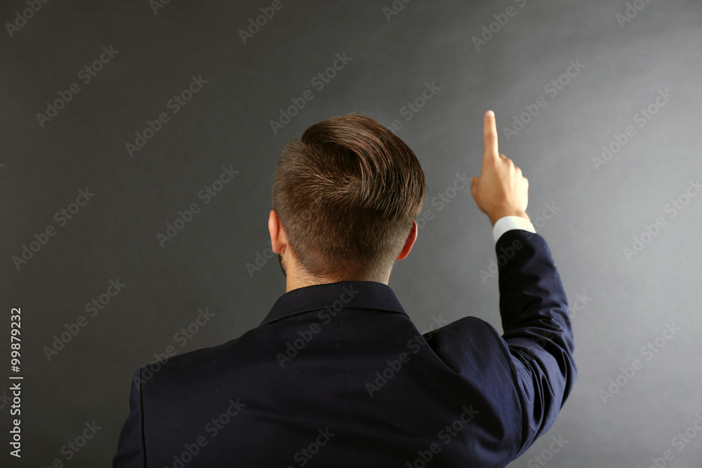 Back view of Caucasian young man in navy blue suit pointing on dark ...