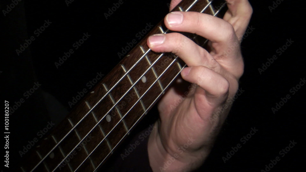 Neck of a bass guitar being played against a black background. Stock ...