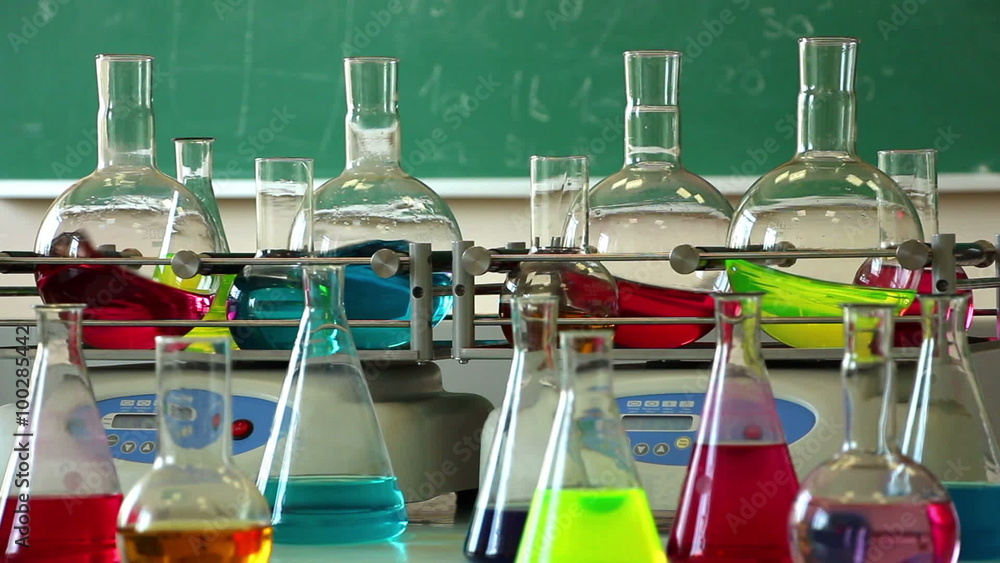 Laboratory shakers agitate eight round glass flasks filled with color ...