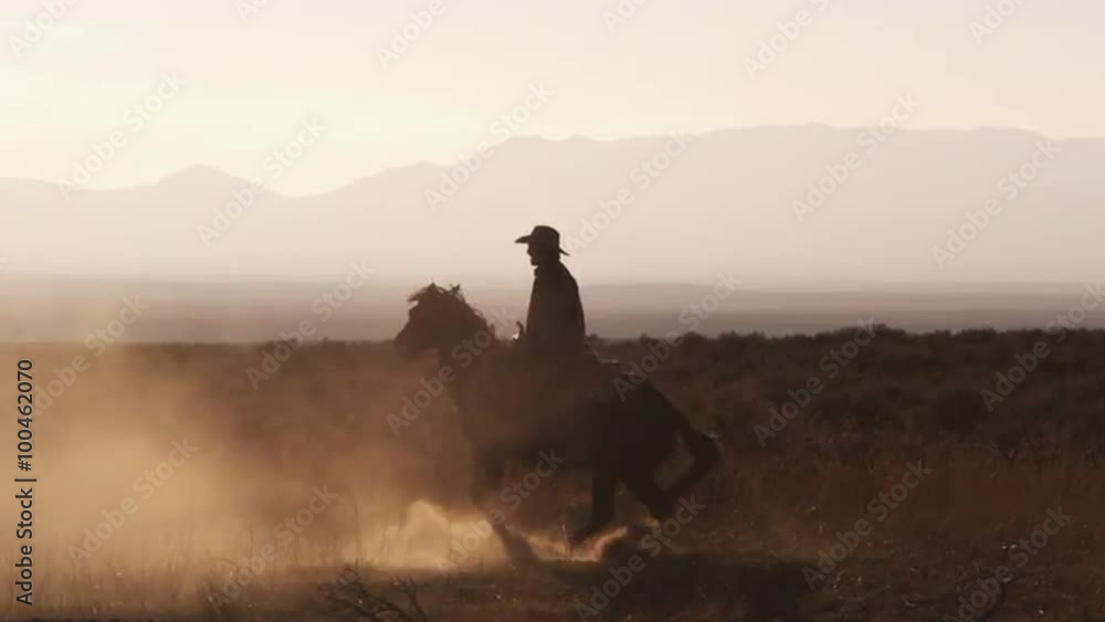 Slow motion silhouette shot of a cowboy riding a hourse in a circle ...