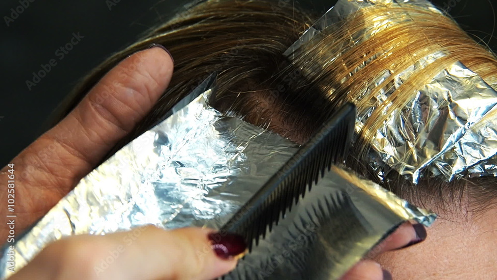 Hairdresser hands folding foil underlay with dyed locks of hair of ...