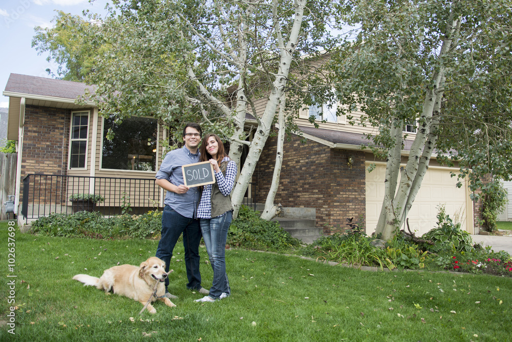Couple And Dog In Front Of New Home With Sold Sign Foto De Stock couple-and-dog-in-front-of-new-home-with-sold-sign-foto-de-stock