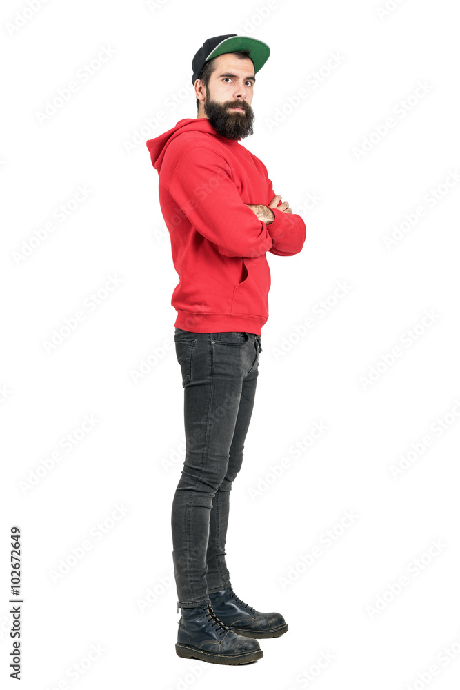 Side view of young bearded man in red hoodie wearing baseball cap with ...
