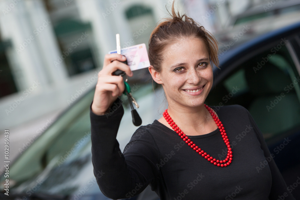 smiling young woman behind the car showing her driver's license and ...