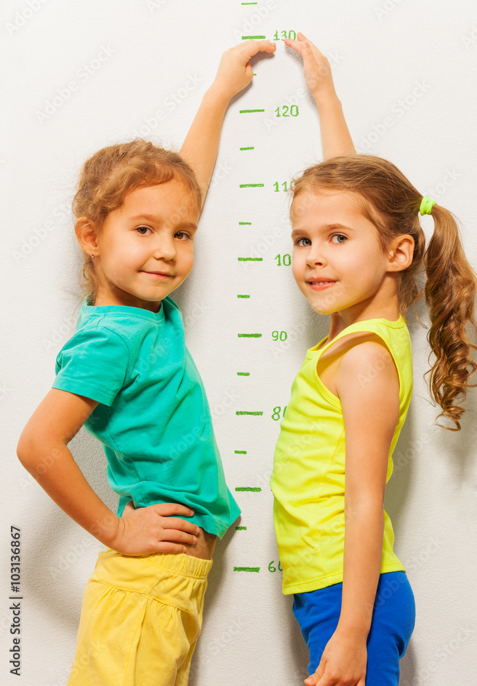Two girls smile show height on wall scale at home Stock Photo | Adobe Stock