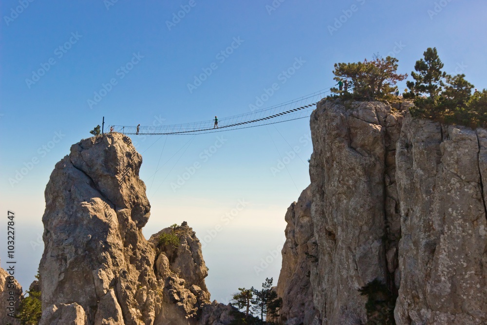 People crossing the chasm on the hanging bridge. Black sea background ...