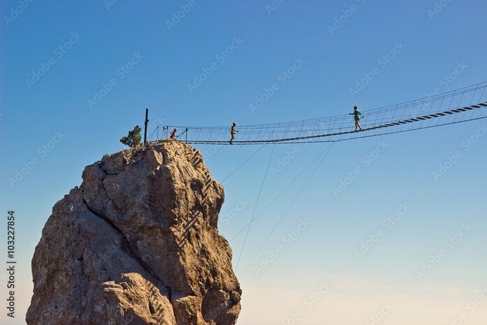 People crossing the chasm on the hanging bridge. Black sea background ...