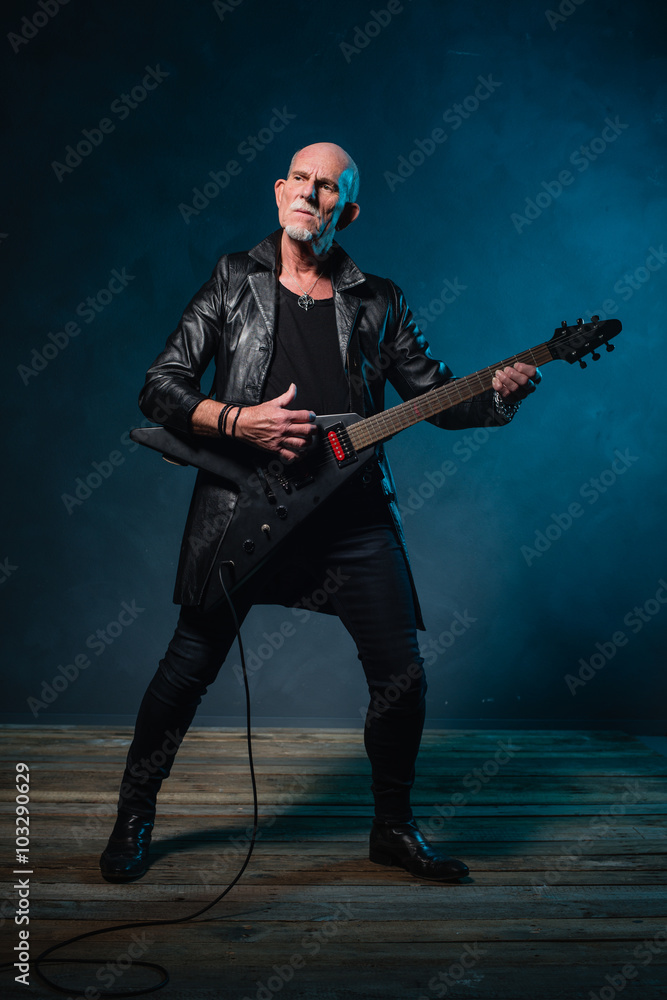 Bald heavy metal senior man with electric guitar in front of dar Stock ...