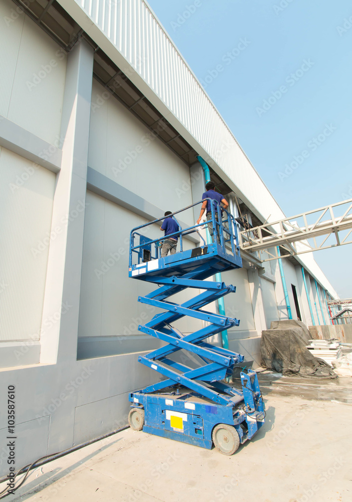 Builder on a Scissor Lift Platform at a construction site. Men at work ...
