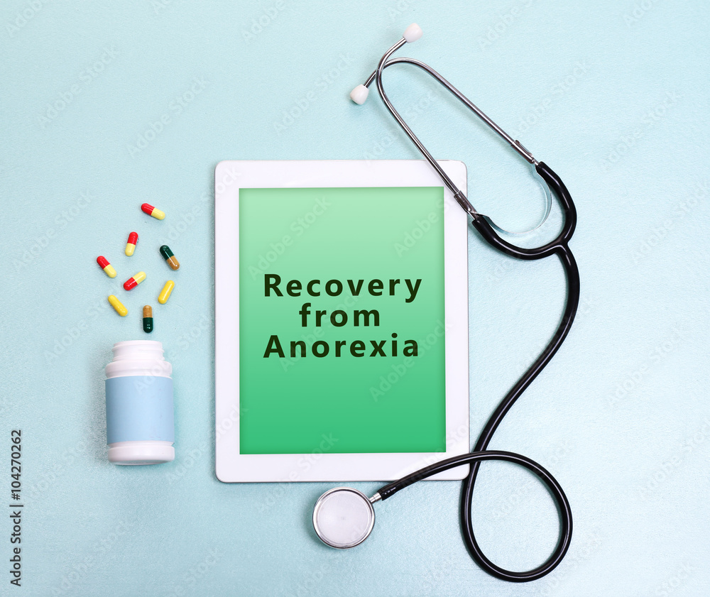 Tablet pc and text Recovery from Anorexia on screen on light blue ...