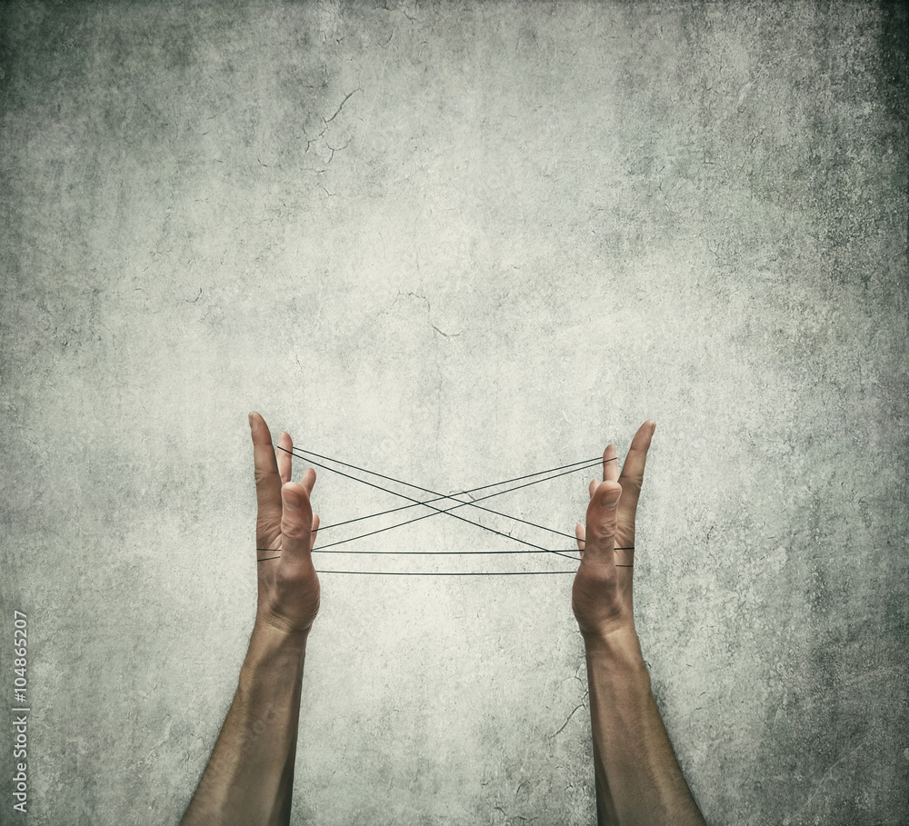 Two human hands playing cats cradle game with a thread on a grey ...