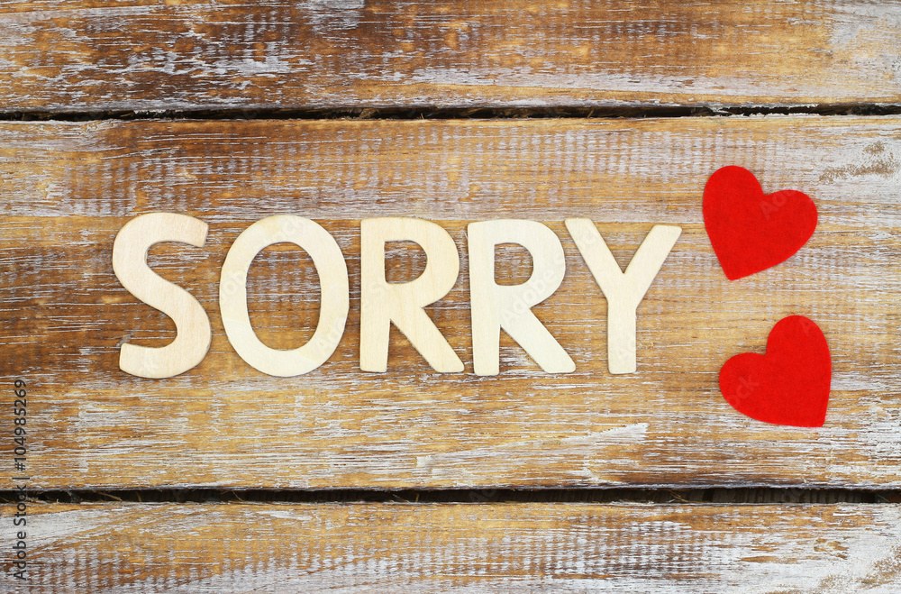 Sorry written with wooden letters and two red hearts on rustic surface ...