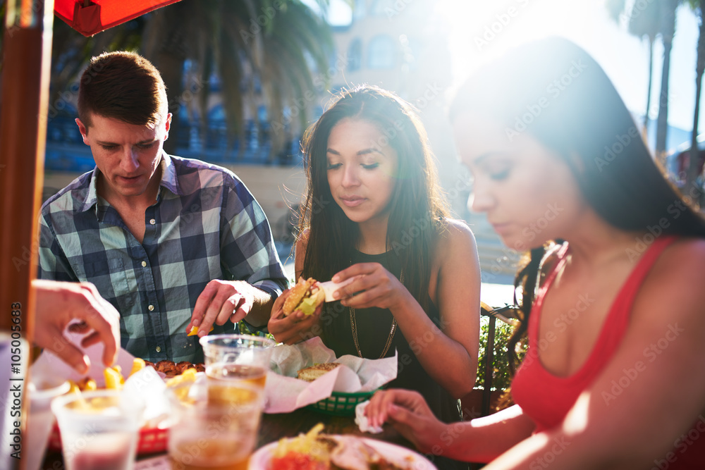 group of three friends eating lunch with beer and food under summer sun ...