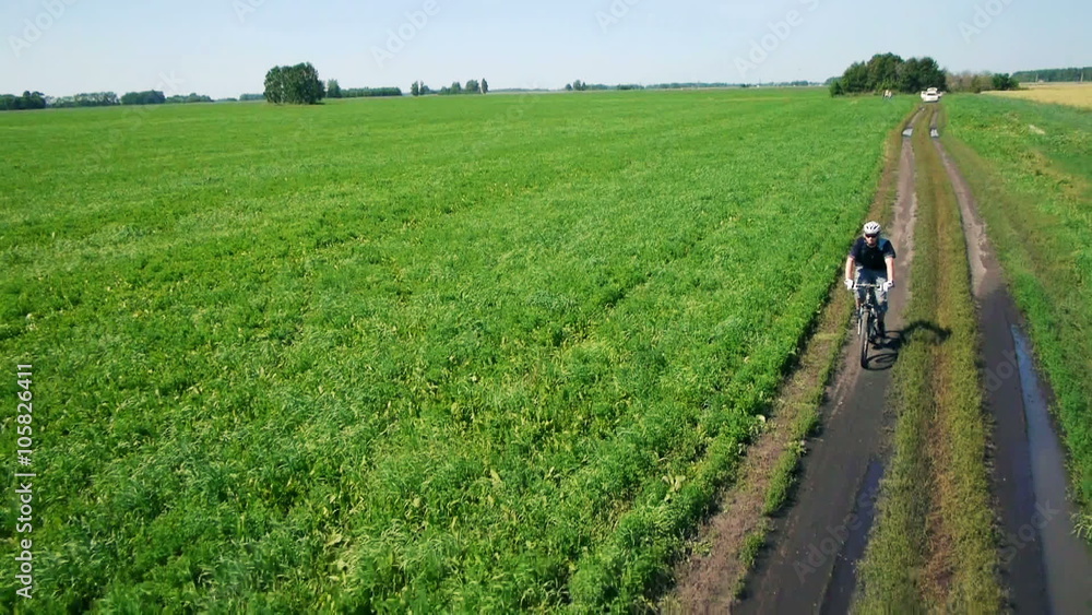 AERIAL: Young man cycling on bicycle at rural road through green and ...