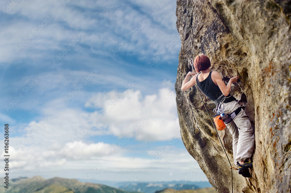 Rear view of young female climber climbing with rope and carbines on a ...