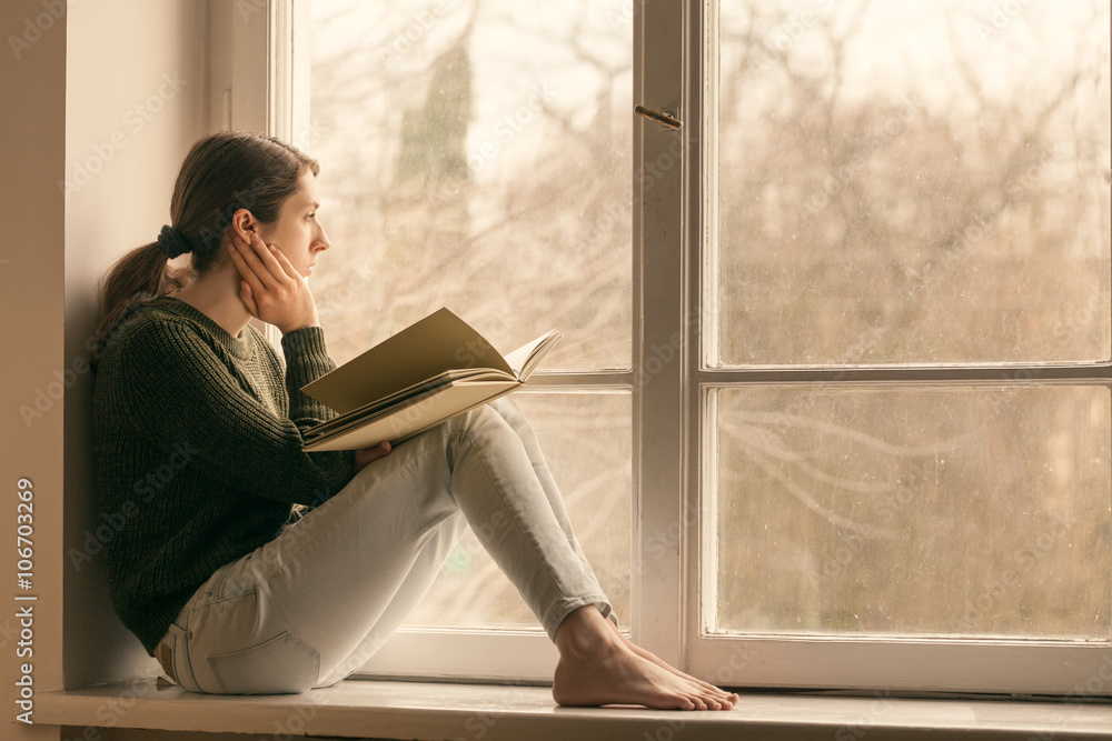 Woman sitting on a window sill, reading and looking through a window ...