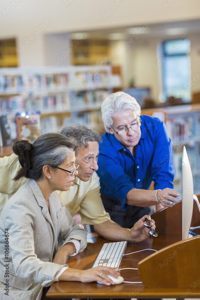 Teacher helping adult students use computer in library Stock Photo ...