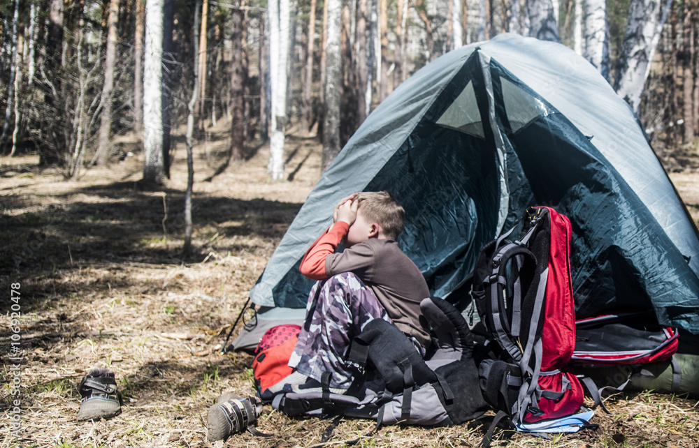Boy with hands over his face sitting outside tent in forest Stock Photo ...