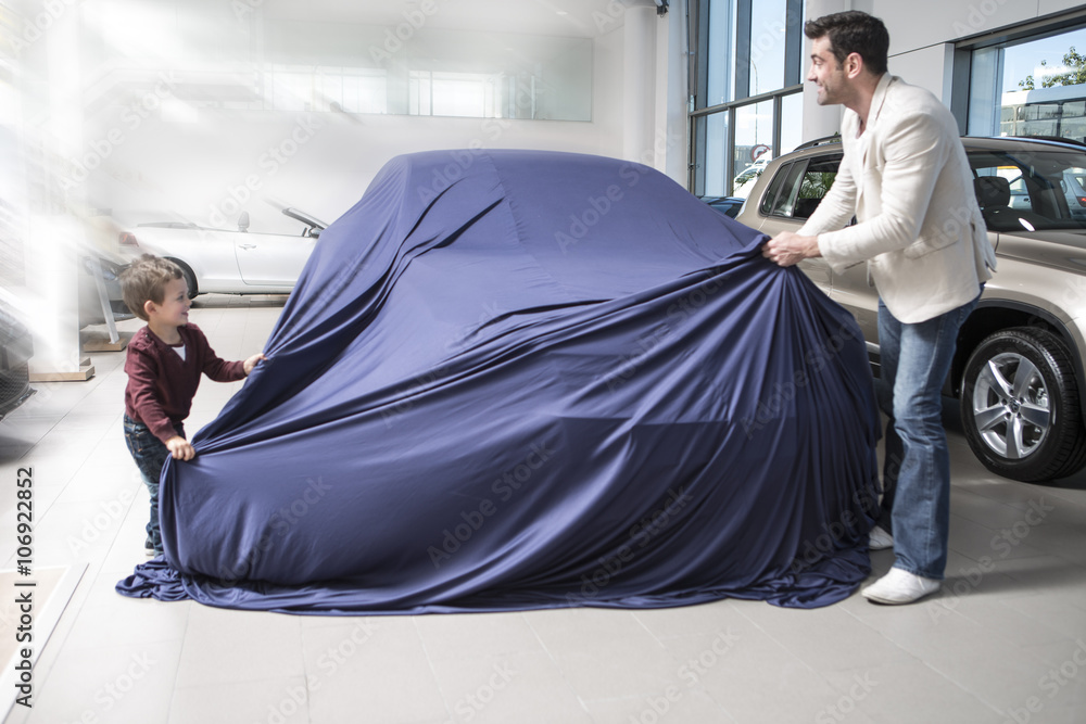 Mid adult man uncovering new car with son in car dealership Stock Photo ...