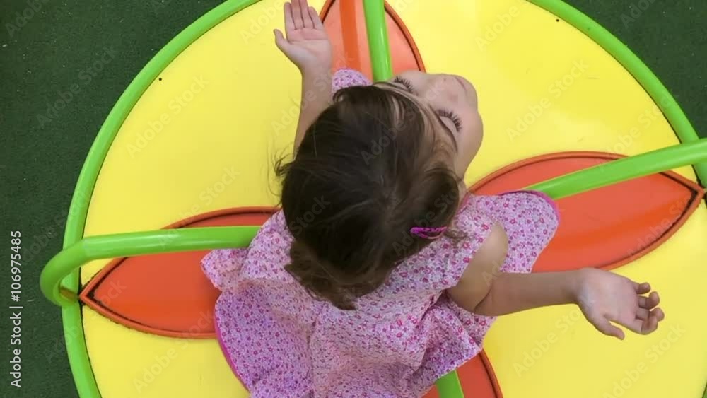 Slow motion and top view of a little girl (age 5-6) sit spin a carousel ...