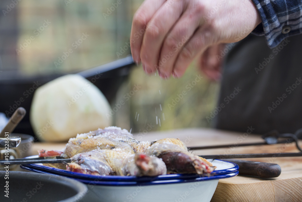A spatchcocked game bird being seasoned for cooking, a man's hand ...