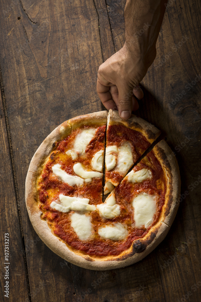 Pizza che viene presa da una mano su tavolo in legno Stock Photo ...