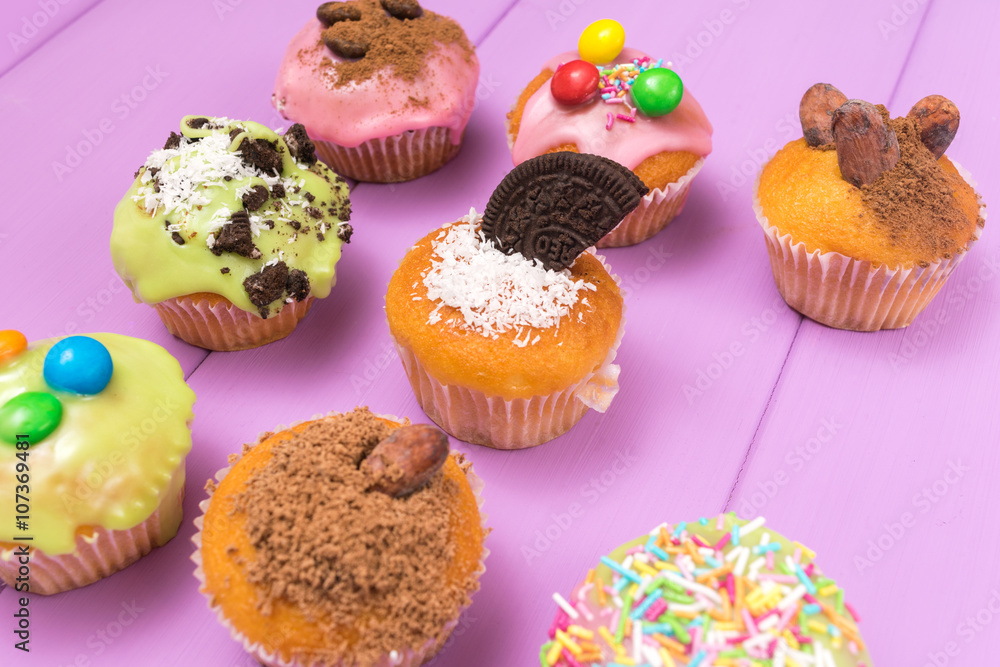 Multiple muffins decorated with mulicolored frosting, cocoa powder and ...