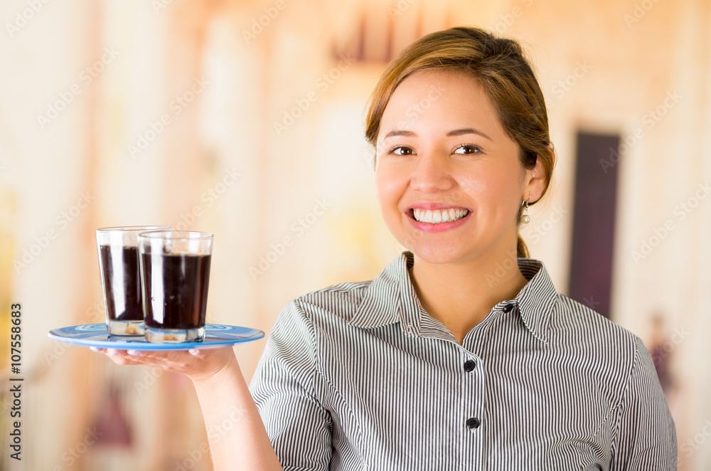 Young brunette waitress wearing uniform with friendly smile, holding up ...
