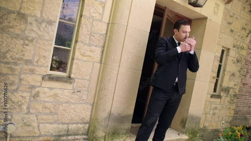 Medium shot of man in a black suit coming out of a large house, takes a ...