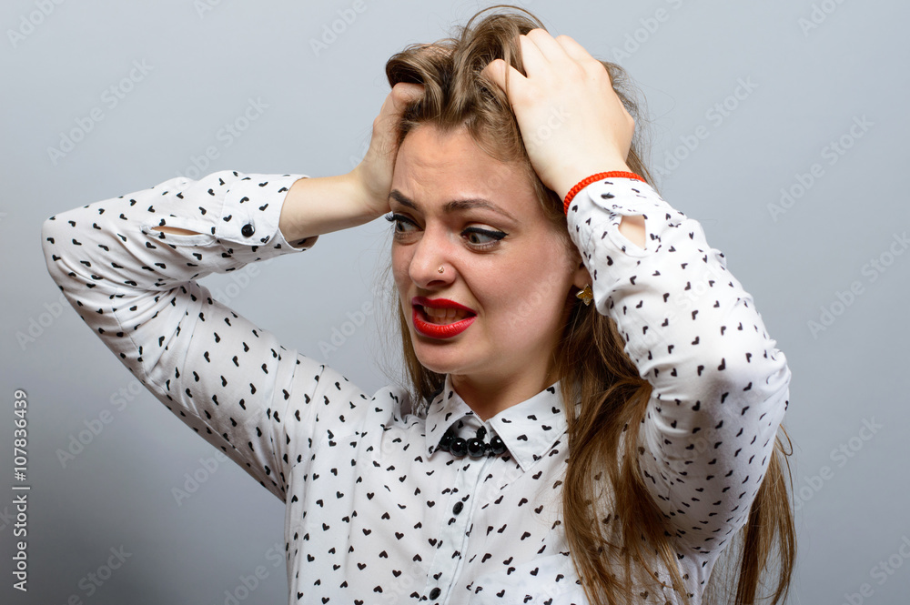 Portrait of a frustrated young screaming woman pulling her hair on gray ...