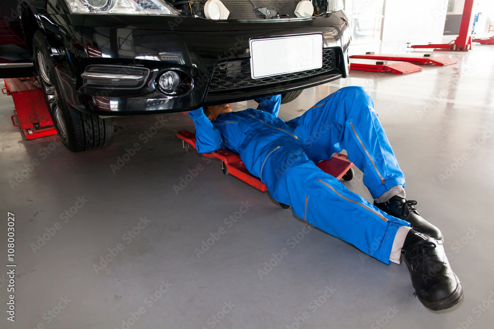 Mechanic in blue uniform lying down and working under car at the Stock ...
