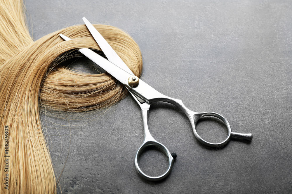 Hairdresser's scissors with strand of blonde hair on grey background ...