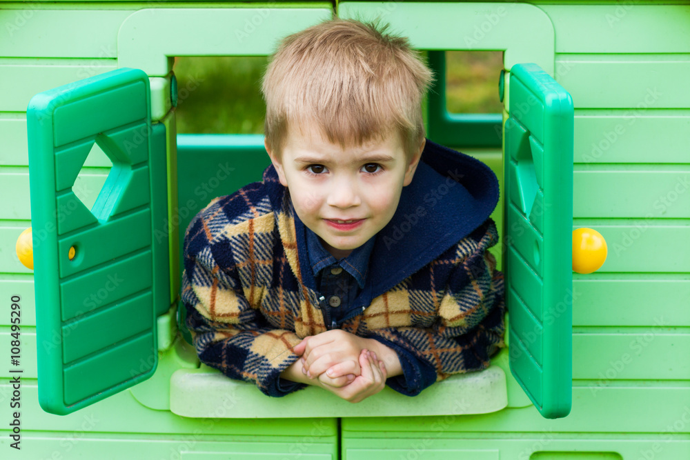 young child looks out of the window of the plastic house, playground ...