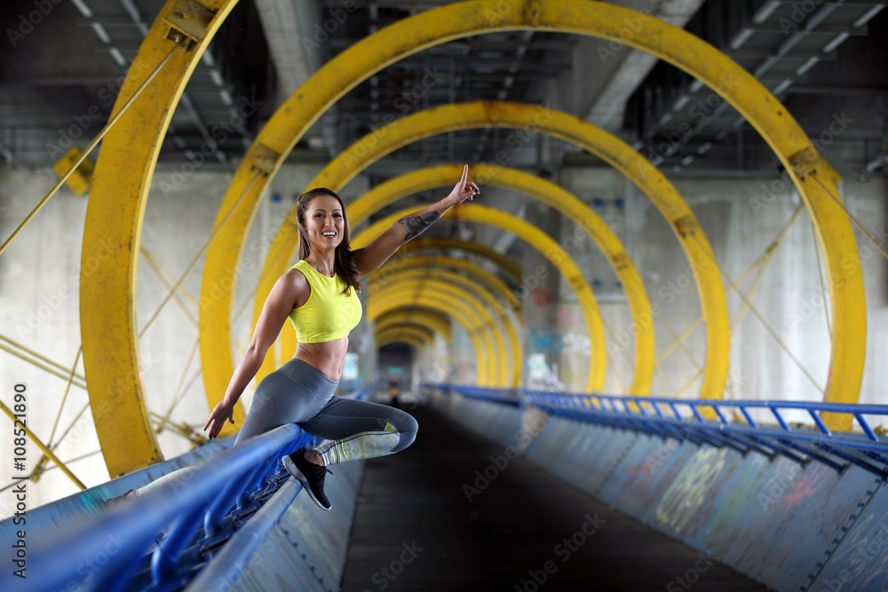 Foto de Sexy fitness girl sitting on the handrail of a bridge do Stock ...