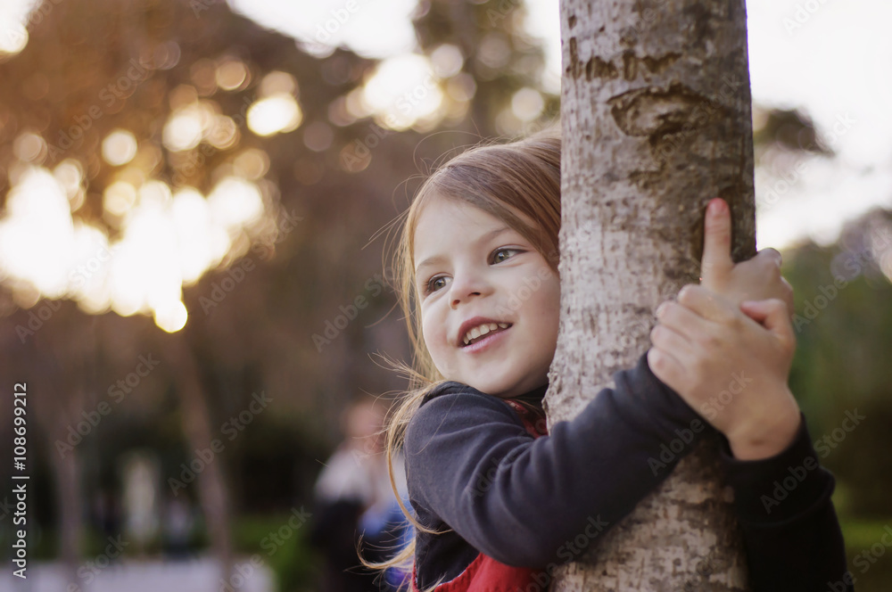 Beautiful little girl smiling, hugging a tree trunk. Little girl Stock ...