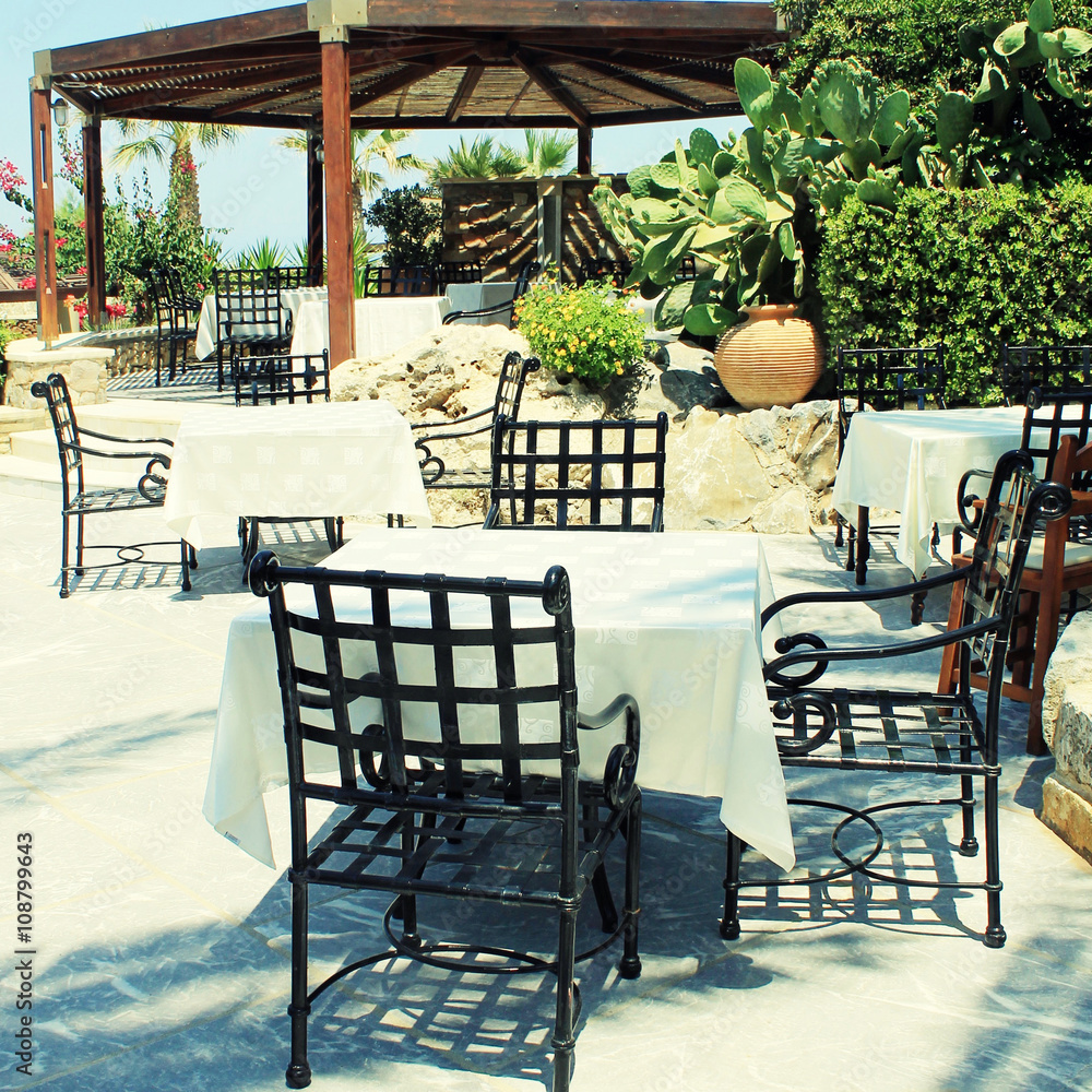 Tables and iron chairs on terrace and beautiful garden, Crete, Greece ...