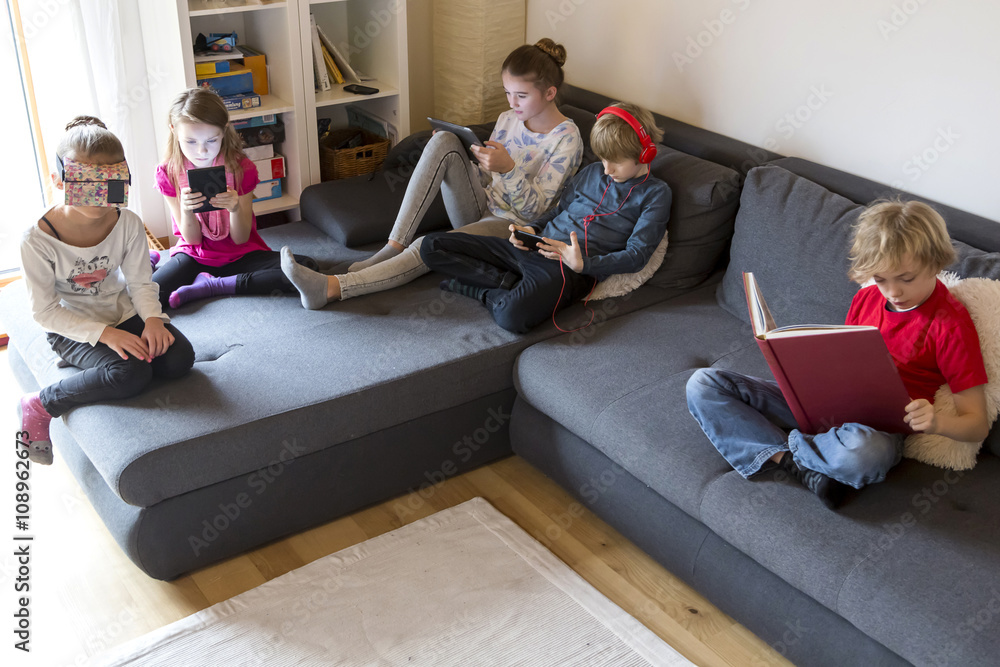 Children using different digital devices while one boy reading a book ...