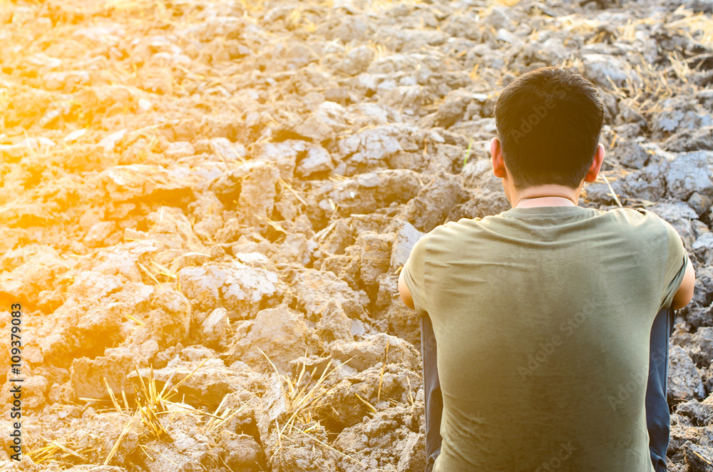 Frustrated and Sad young man sitting on barren ground. Look for a dry ...