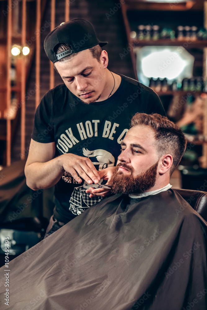 Young handsome barber making beard grooming of attractive bearded man ...