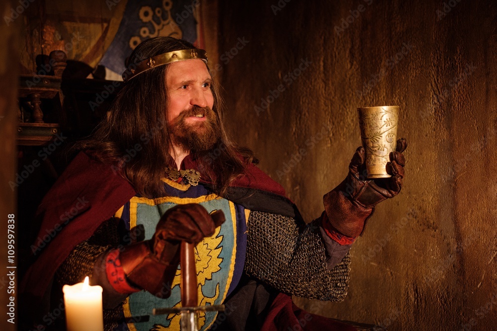 Old medieval king with goblet of wine on the throne in ancient castle ...
