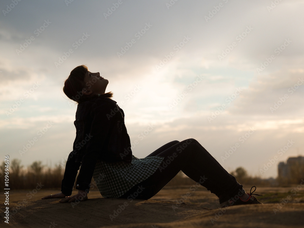 Young teen girl sitting on the ground and looking up at the sky. The ...