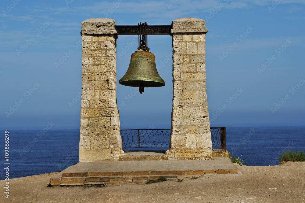 Big bell between two stone pillars on the beach with blue sea ...