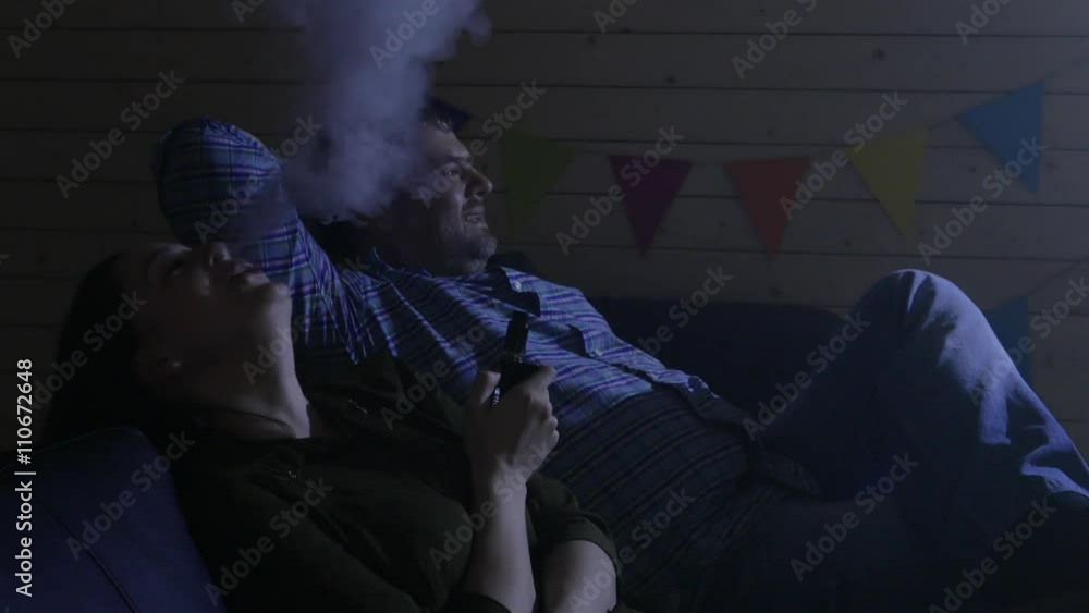 A couple vaping, inhaling and exhaling large clouds of smoke and having ...