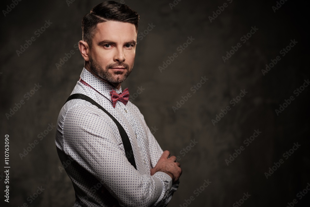 Stylish man with bow tie wearing suspenders and posing on dark ...