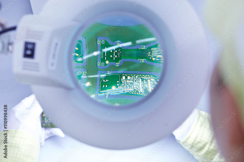 Young woman using magnifier at quality check station at factory ...