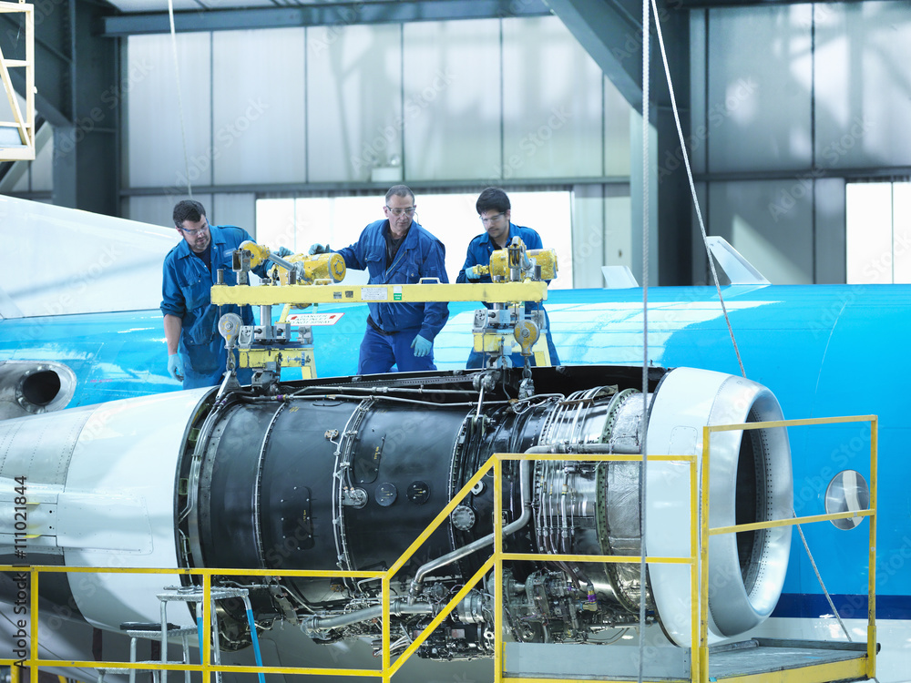 Engineers removing jet engine from aircraft in aircraft maintenance ...
