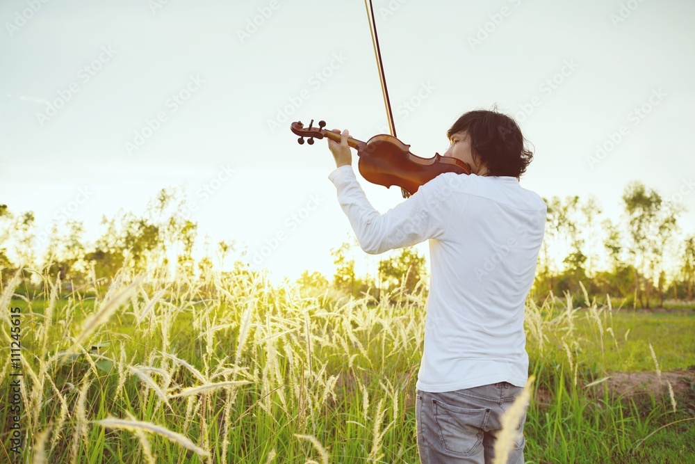 Young man playing the violin at sunrise standing with his backside to ...